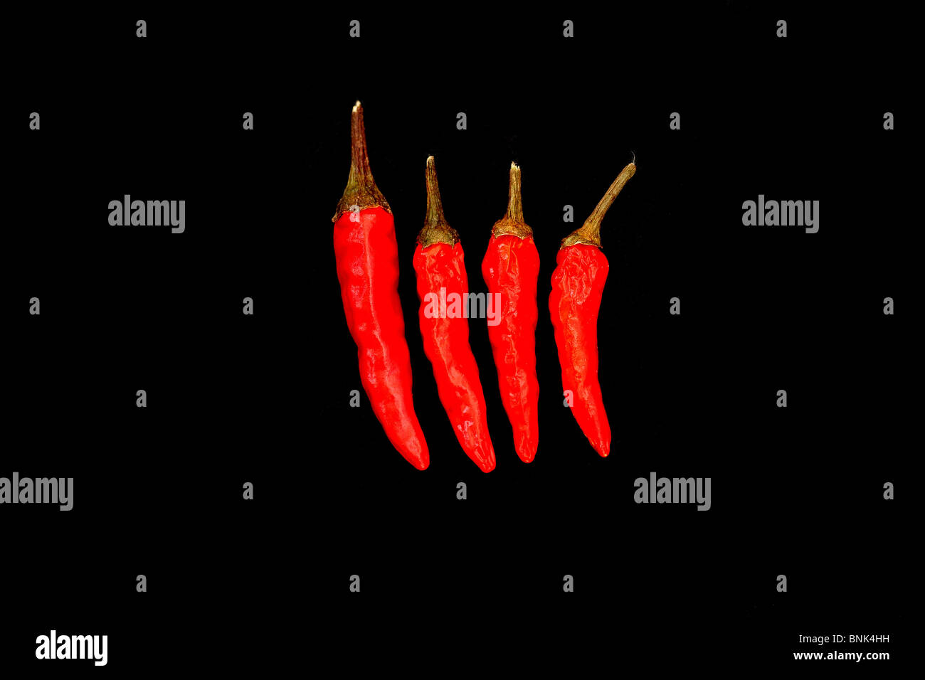 4 hot red chilli's on a black background Stock Photo - Alamy