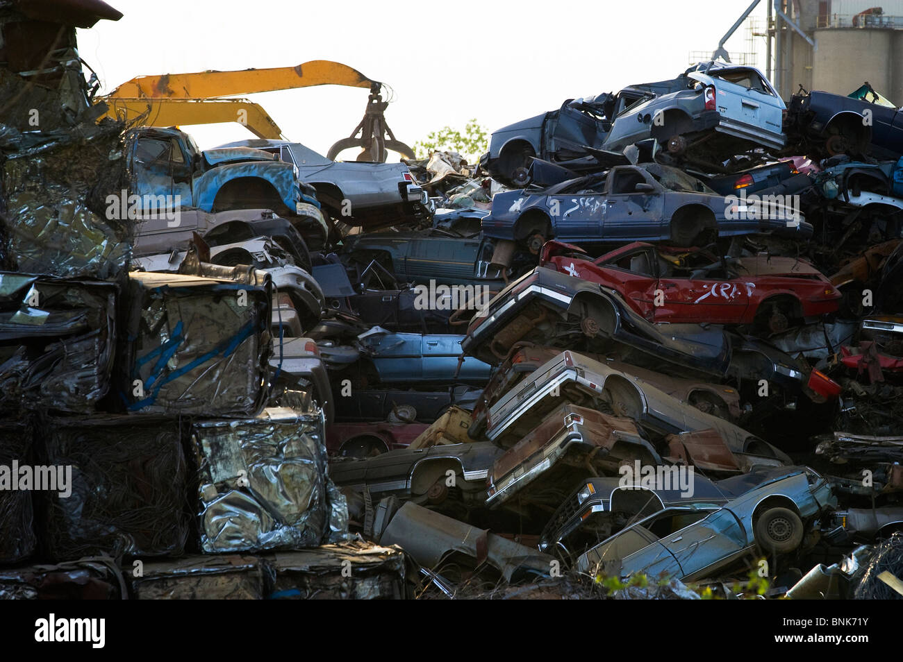 Crushed aluminum bales and scrap cars piled high with yellow cranes ...