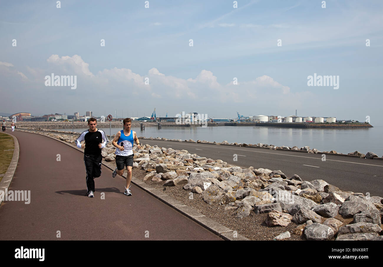 Two men running training on barrage across Cardiff Bay Wales UK Stock ...