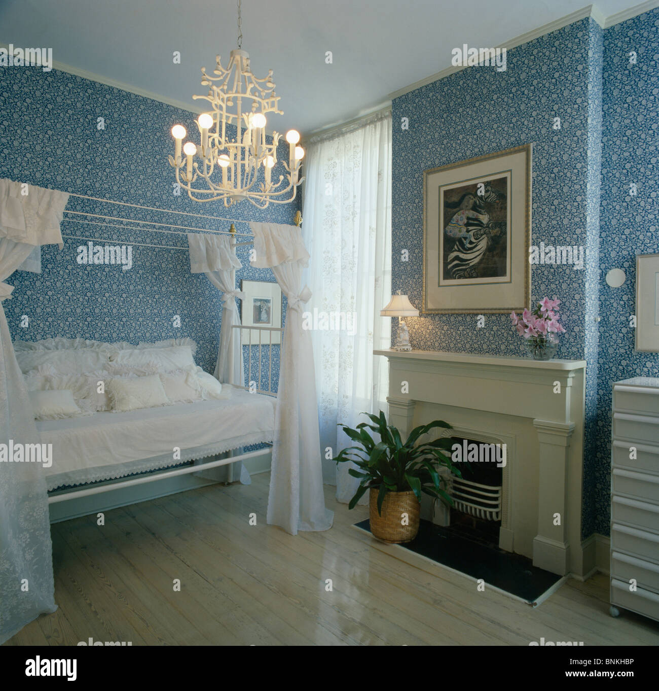 Chandelier above white bed with white bedlinen and drapes in bedroom ...