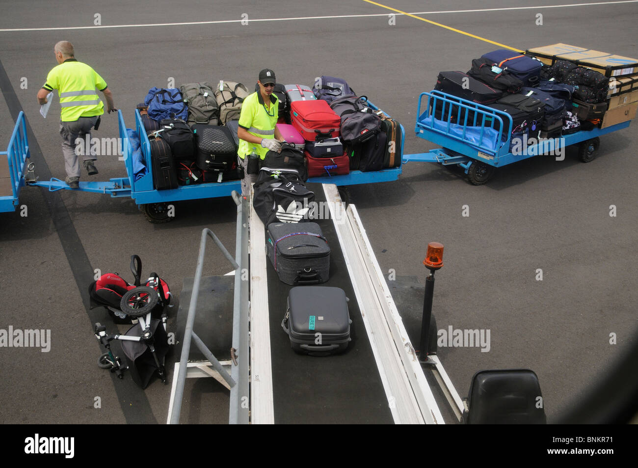 Airport baggage handler loading bags from a trolley onto an aircraft at ...