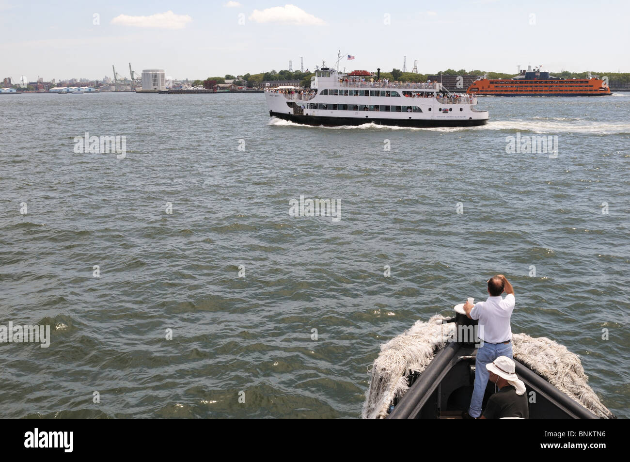 Two ferries traverse New York harbor as people watch from the deck of a ...