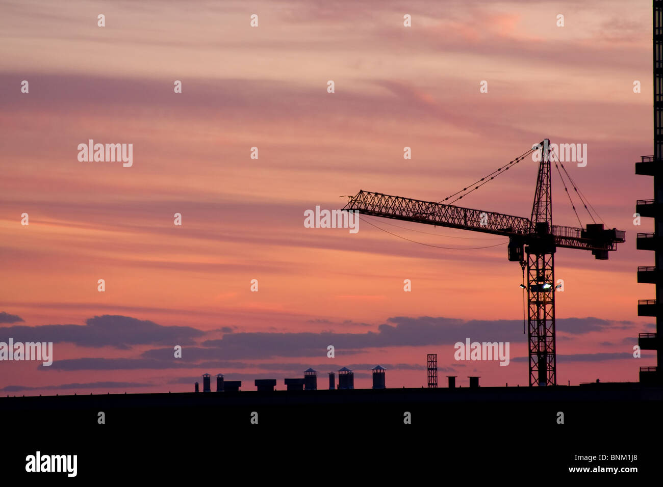 A construction crane over a rooftop at sunset Stock Photo - Alamy