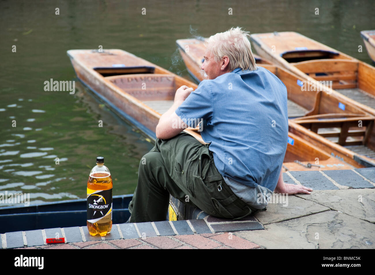 Man sitting on quayside next to parked punts at Cambridge smoking a ...