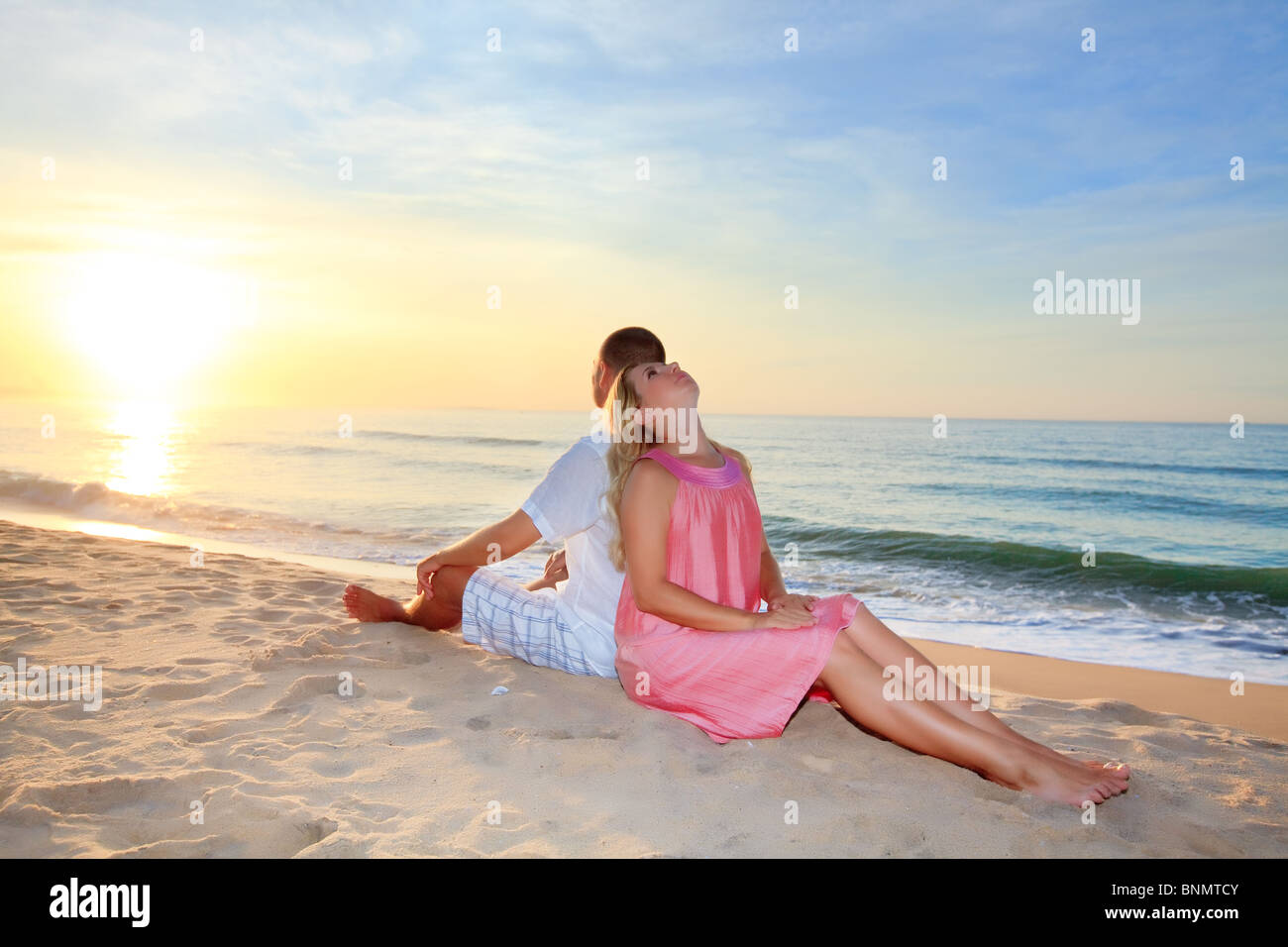 Couple sitting on the beach at sunrise time Stock Photo - Alamy