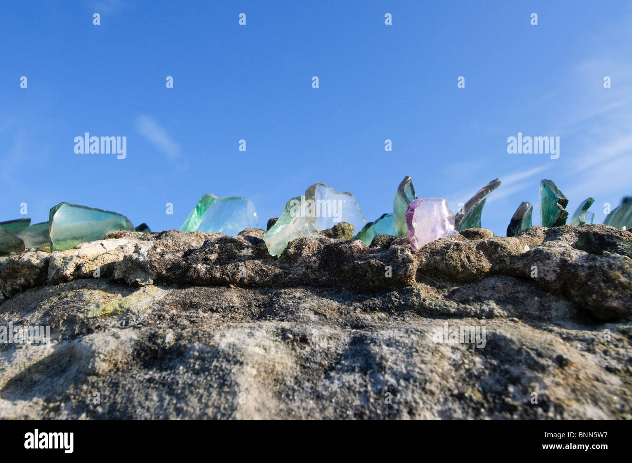 Sharp, broken glass cemented to the top of a stone wall to stop ...
