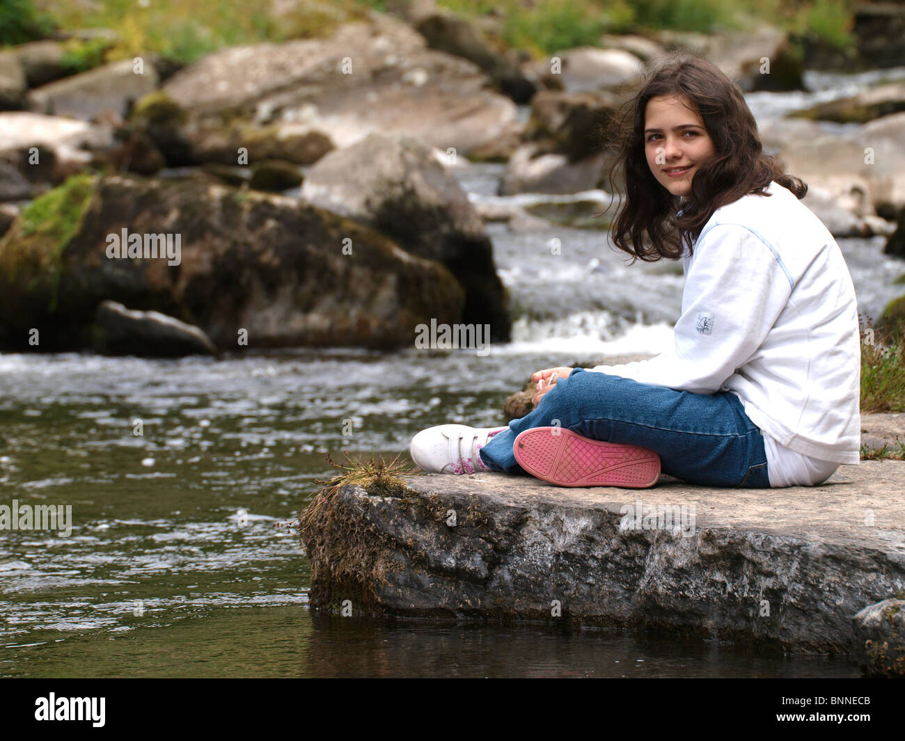 Young girl sat on a rock beside the East Lyn river, Lynmouth, Devon, UK ...