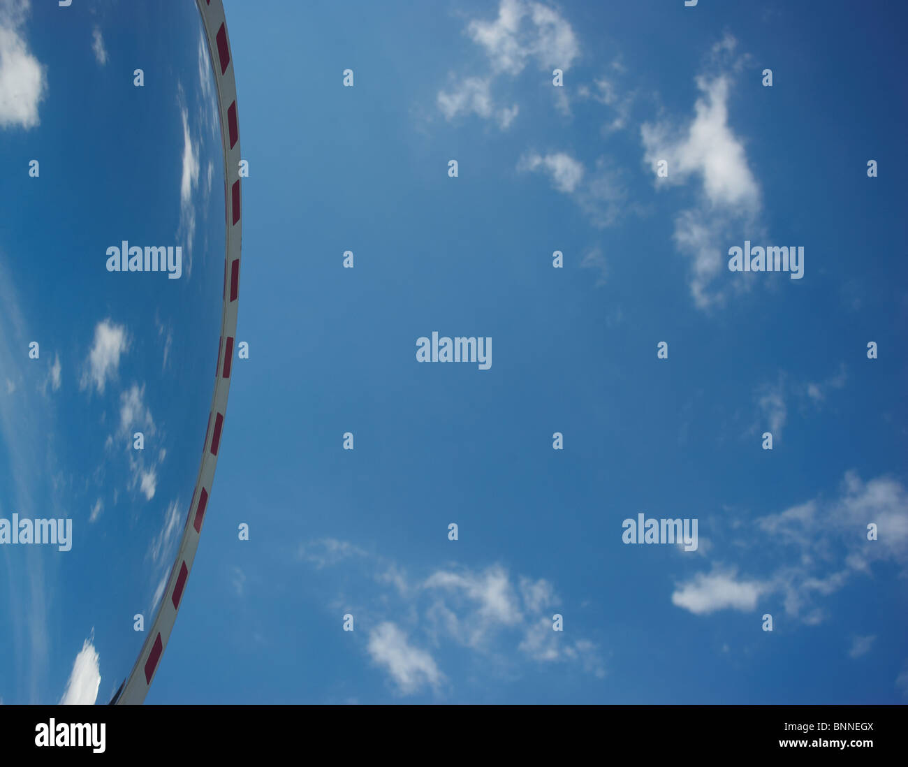 Roadside mirror beneath blue sky with clouds reflecting a portion of ...