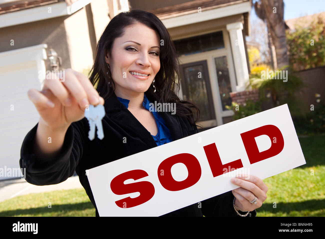 Happy Attractive Hispanic Woman Holding Keys and Sold Sign In Front of ...