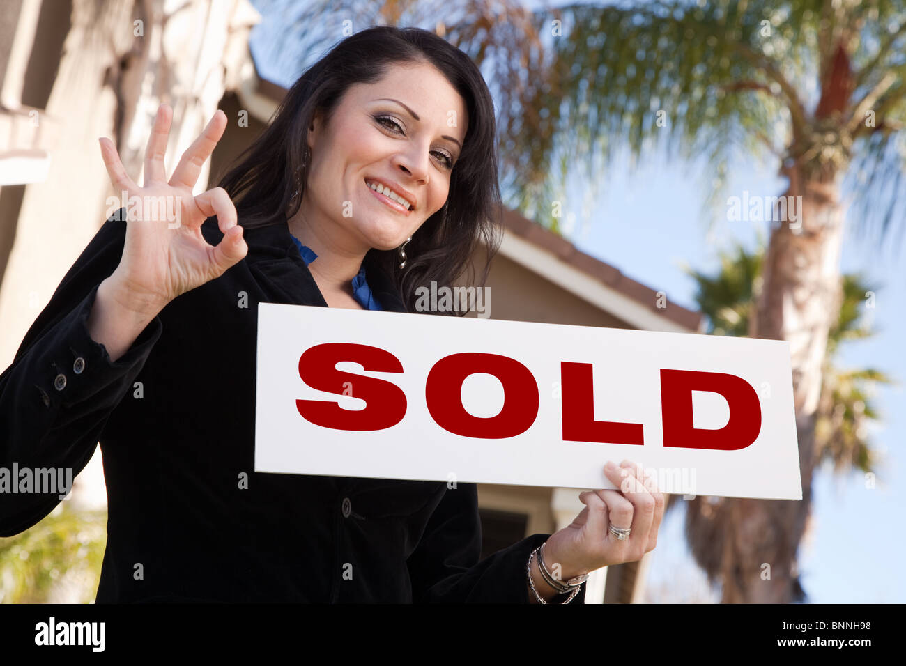 Happy Attractive Hispanic Woman Holding Sold Sign In Front of House ...