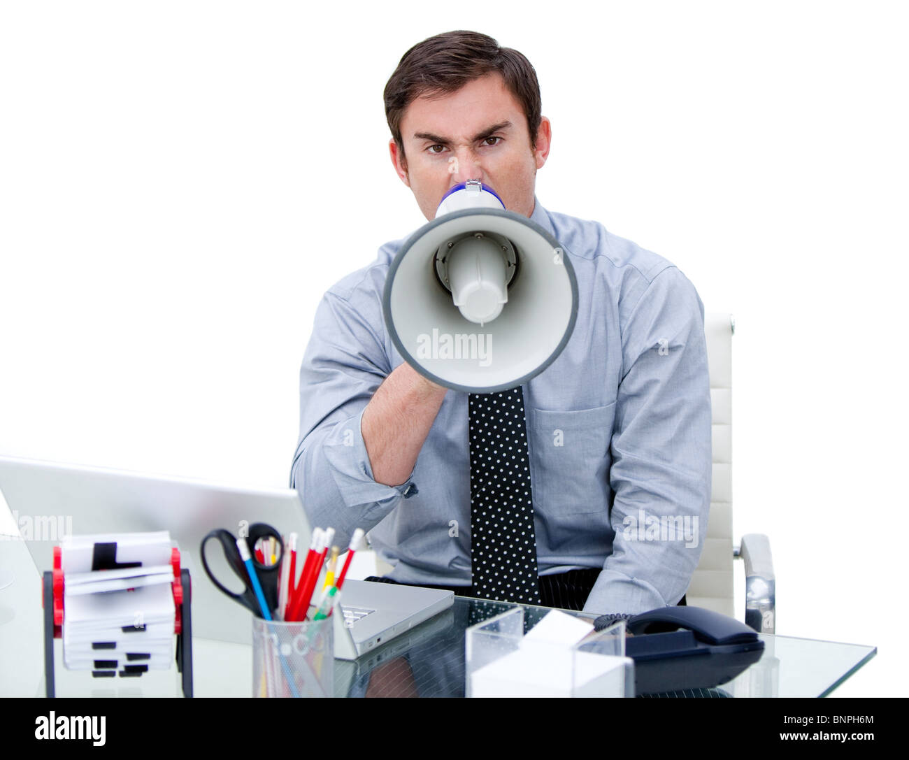 Furious businessman yelling through a megaphone sitting at his desk ...