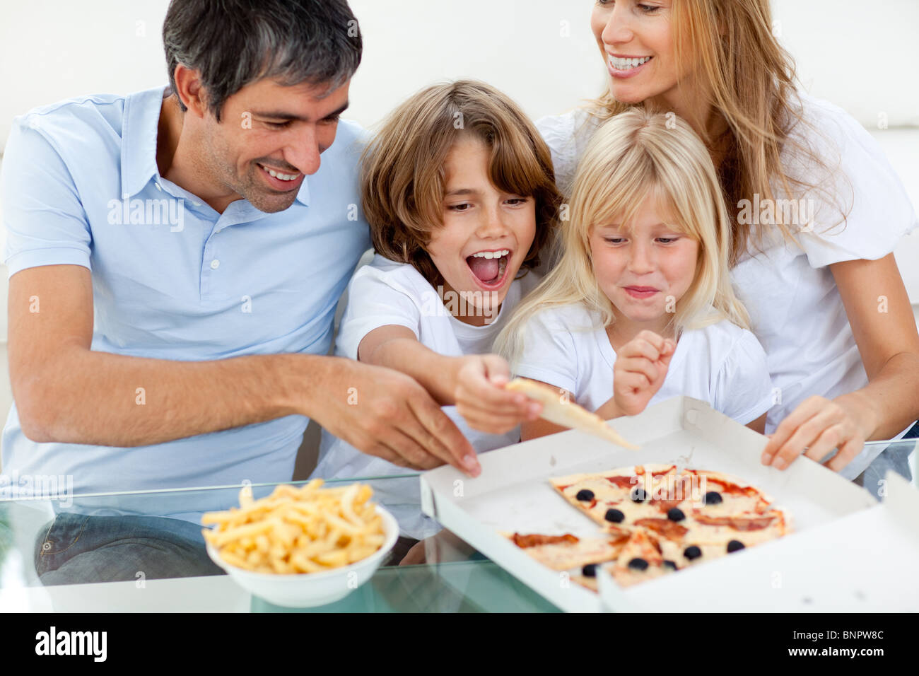 Excited children eating a pizza with their parents Stock Photo - Alamy