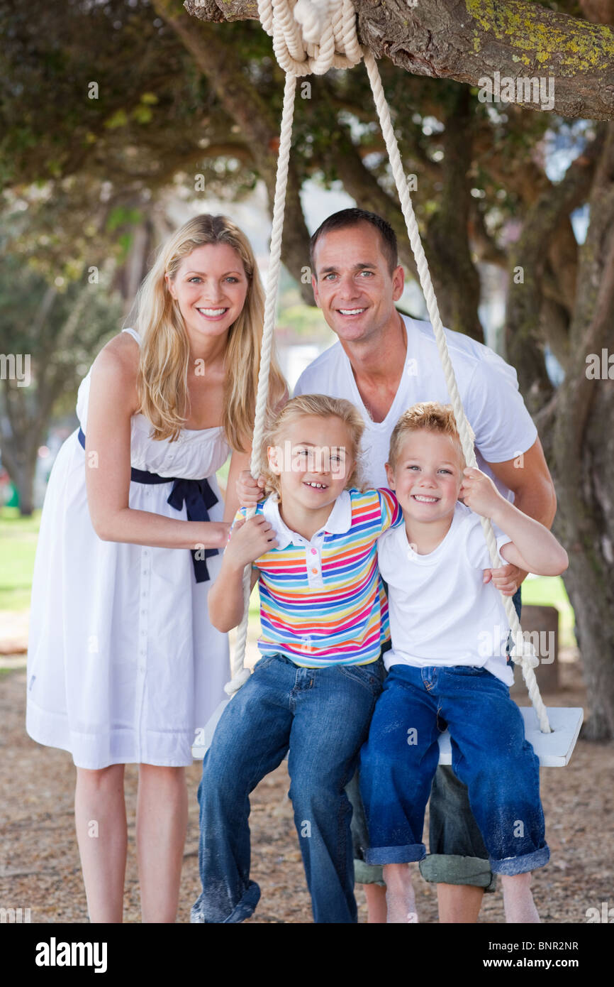 Attentive parents pushing their children on a swing Stock Photo - Alamy