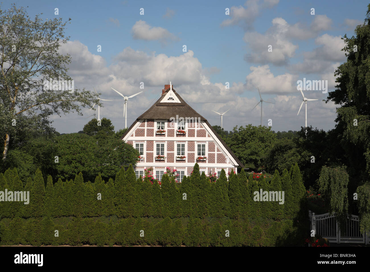 A half timbered thatched farmhouse with a wind farm in the background ...