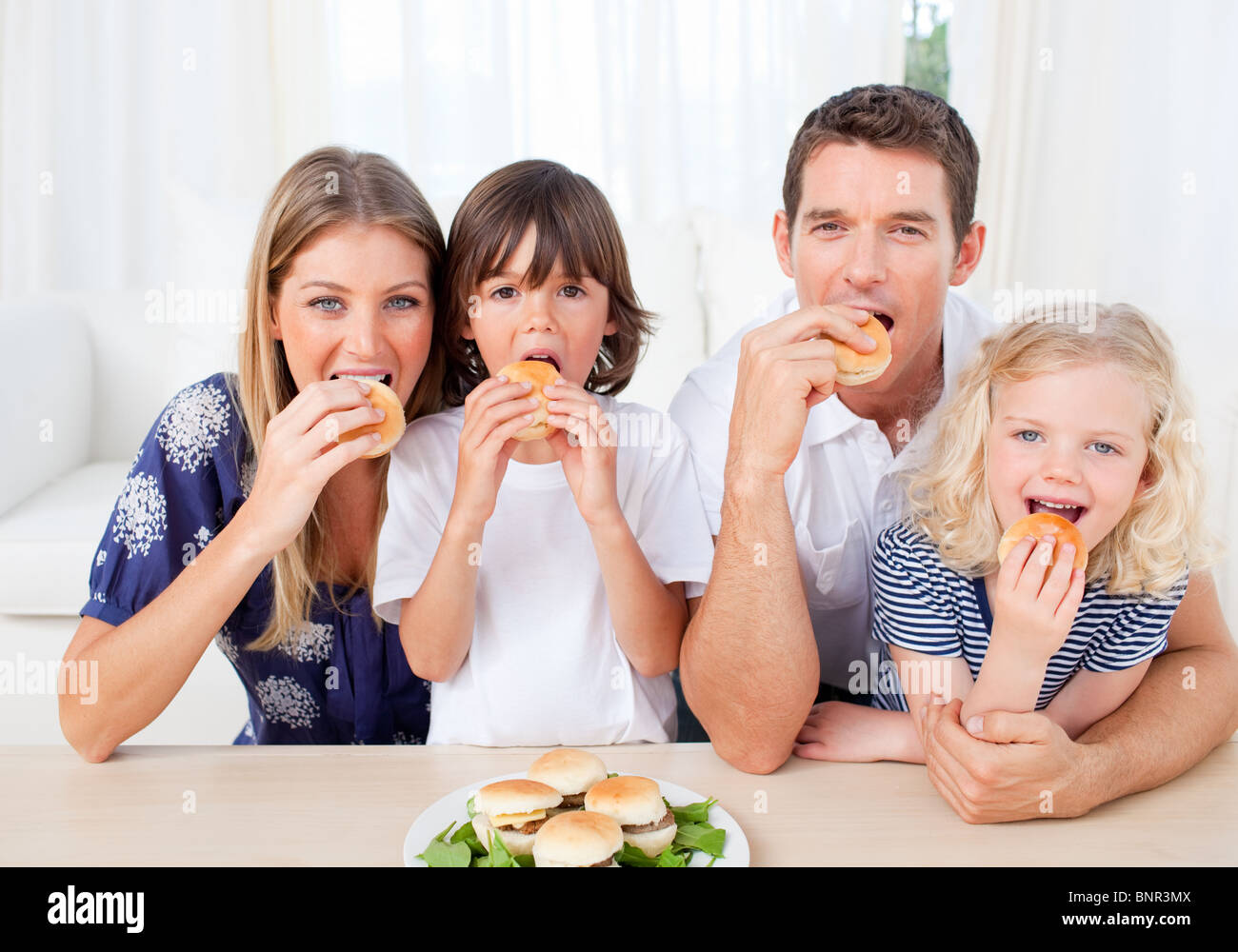 Hungry family eating burgers in the living room Stock Photo - Alamy