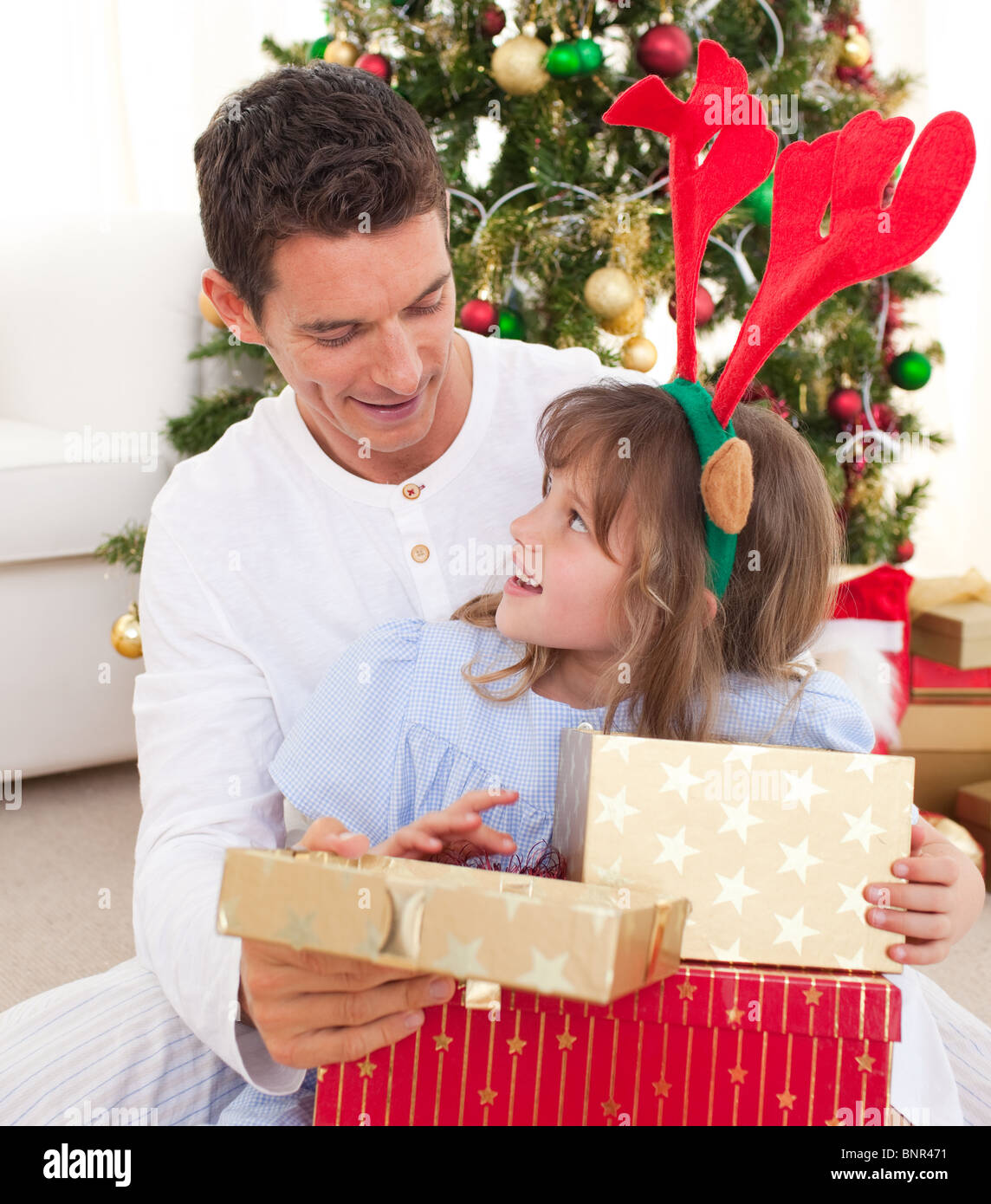 Portrait of a smiling father and his daughter opening Christmas ...