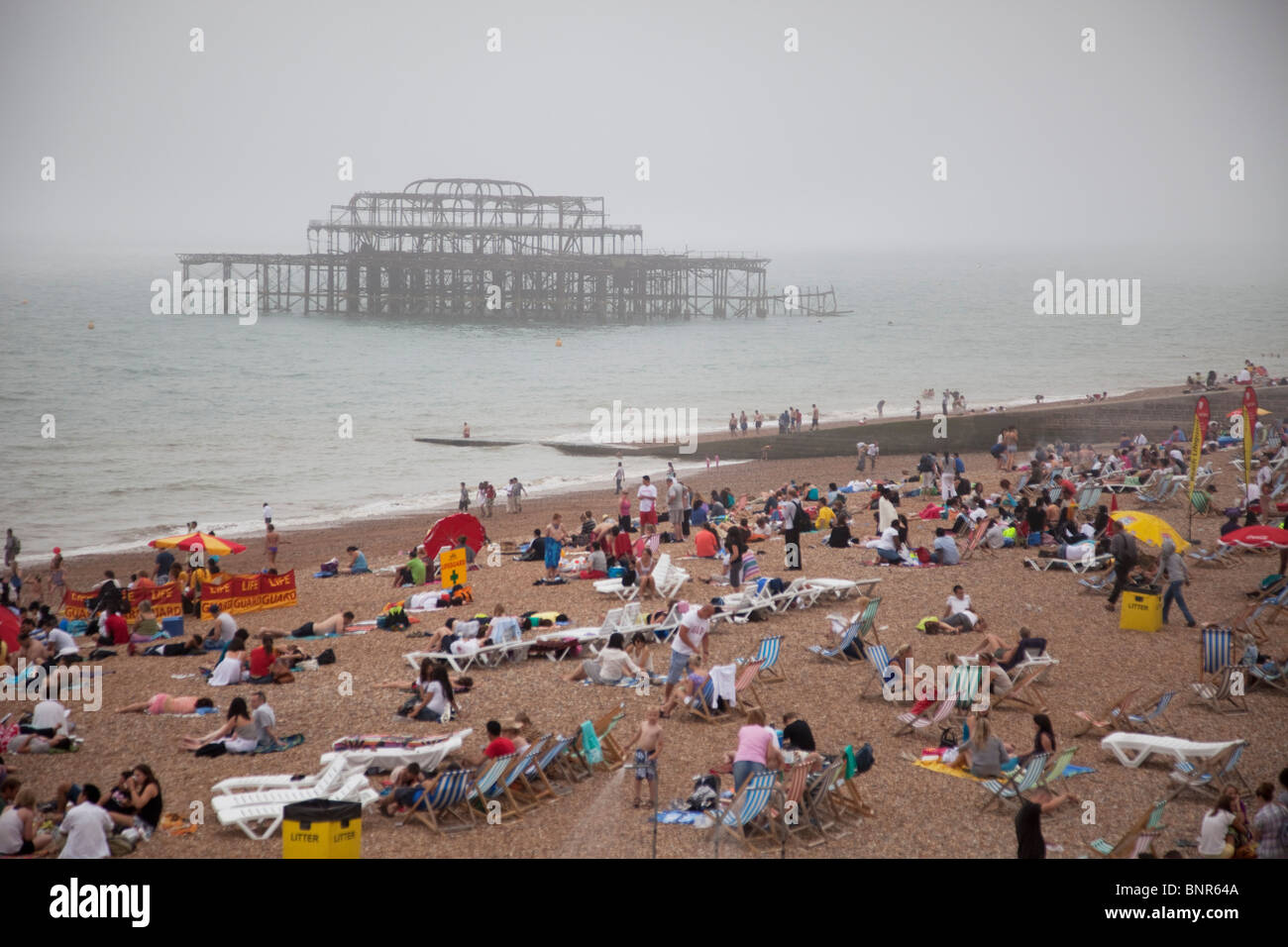 People on Brighton Beach on a misty day. The famous derelict West Pier ...