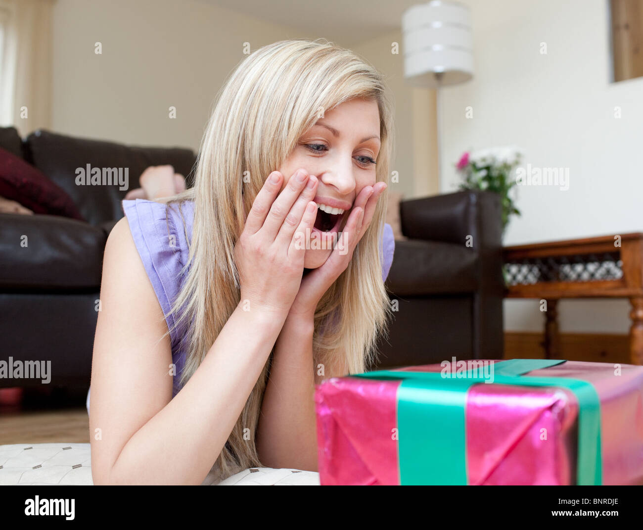 Surprised woman opening gifts lying on the floor Stock Photo - Alamy