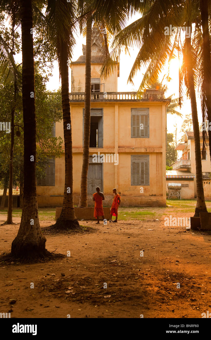 Two Buddhist monks chatting under palm trees near a colonial building ...