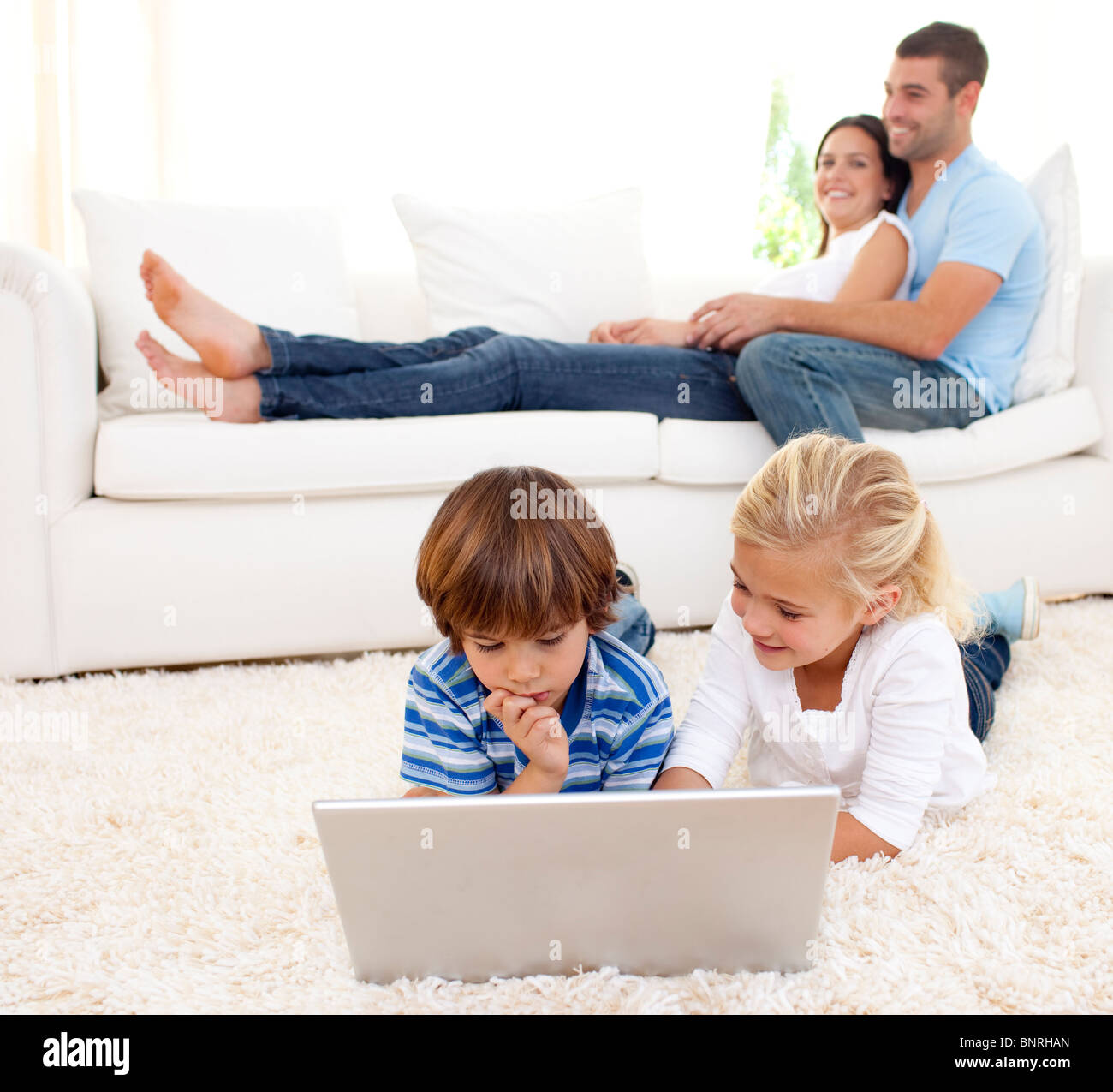 Children using a laptop and parents lying on sofa Stock Photo - Alamy