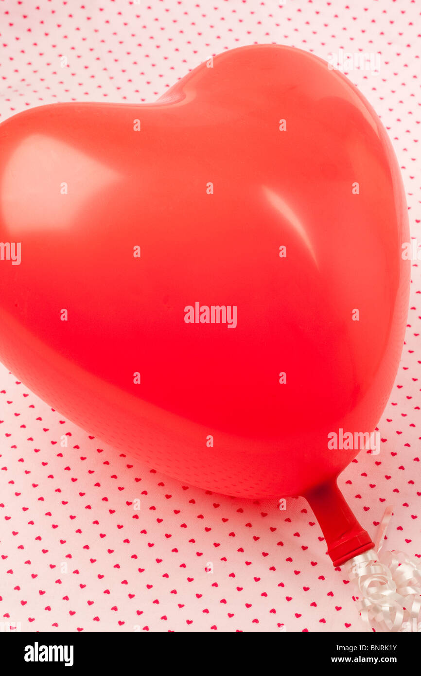 A red heart shaped balloon on a light back ground of small pink hearts ...