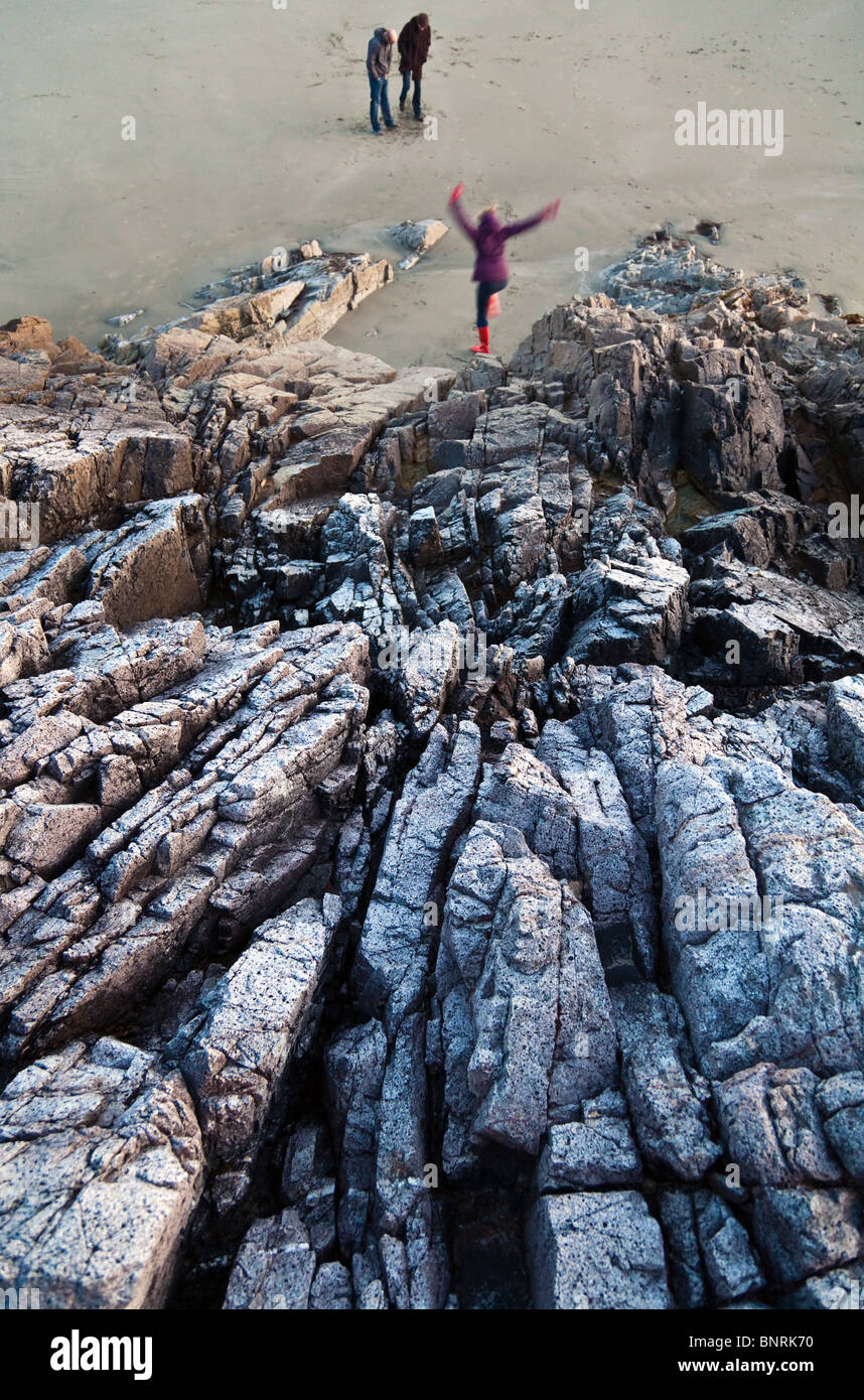 A group of friends wander at the foot of coastal rocks on a beach in ...