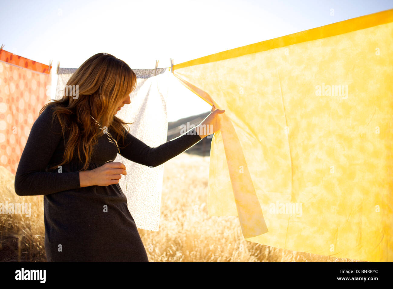 Female moves a yellow sheet hanging on a clothes line to look at what ...