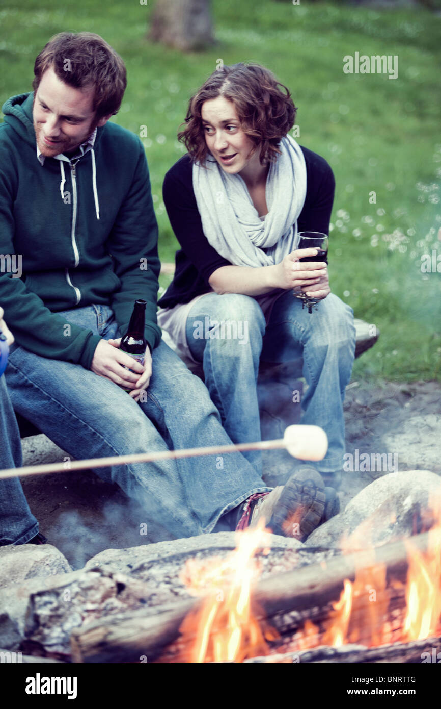 Two friends enjoying beverages sit around and talk at a camp fire ...
