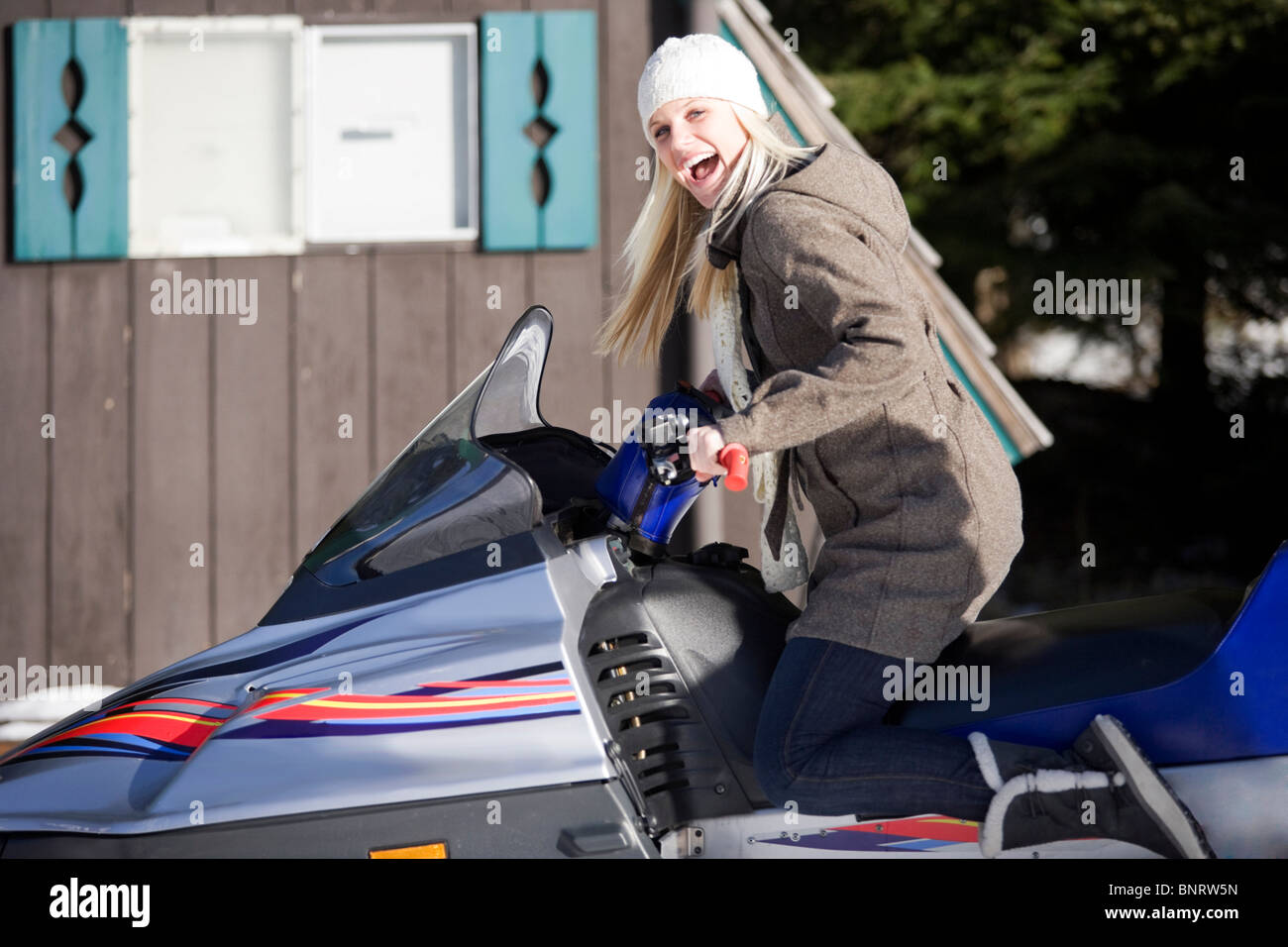 A young woman on a snowmobile seen outside of a rustic mountain cabin ...