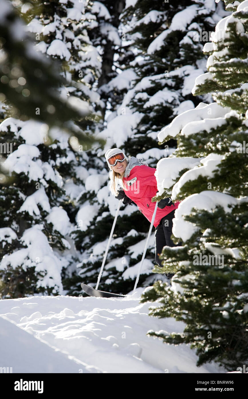 A woman peeks out from behind a branch as she skis among snow flocked ...