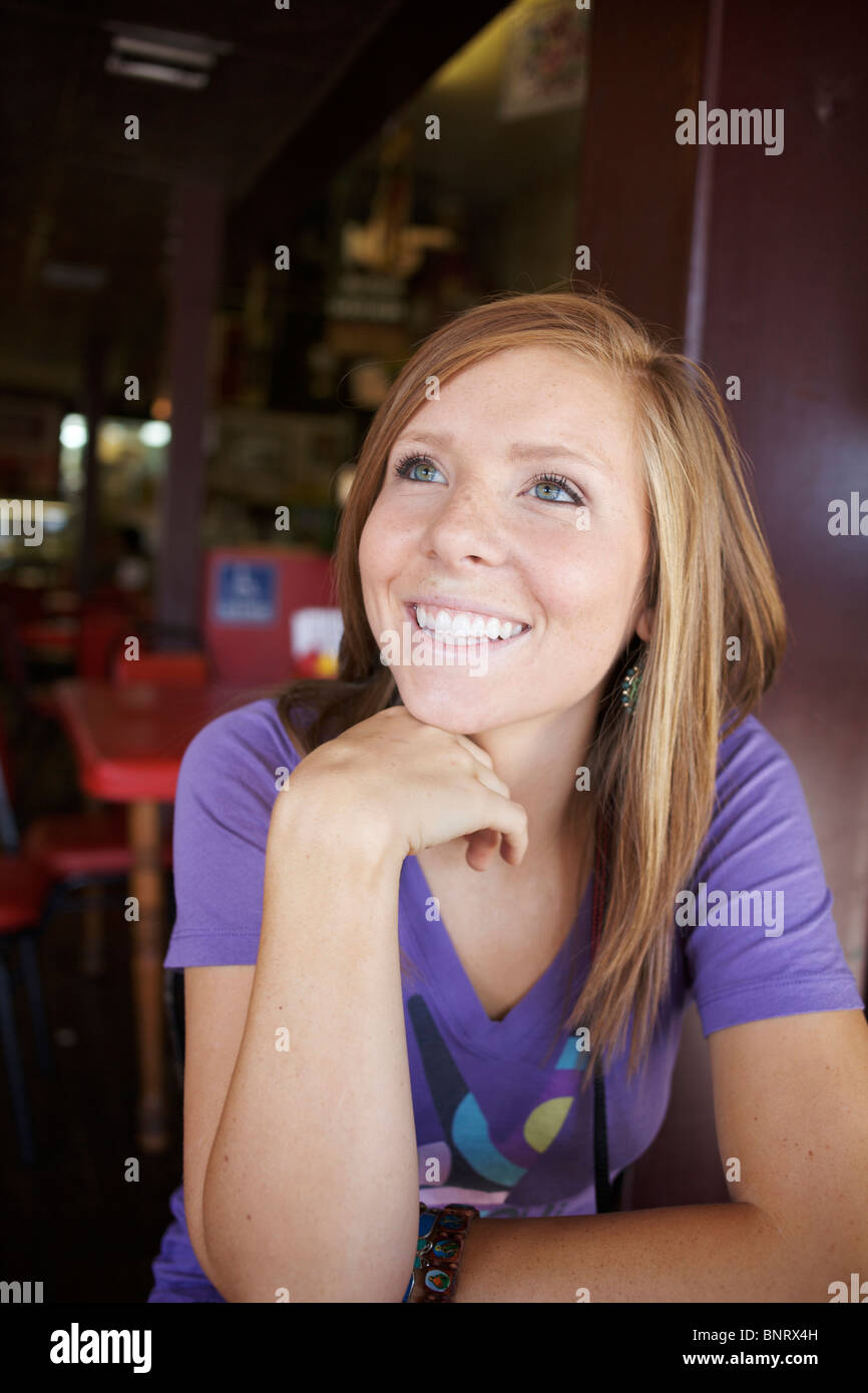 Young, woman sitting in a diner looks away and smiles Stock Photo - Alamy