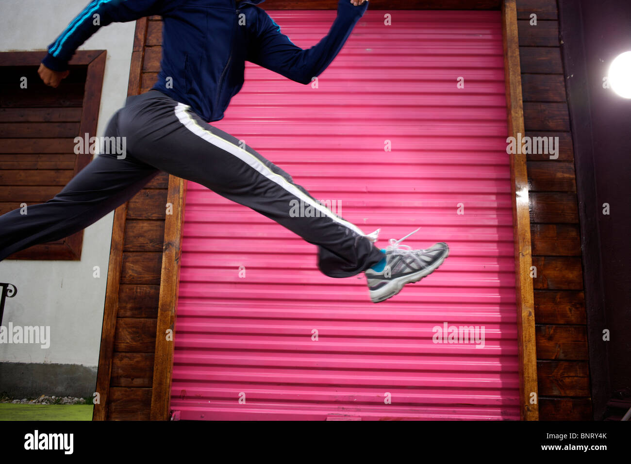 Legs and lower body of a female runner leaping with a pink door in the ...