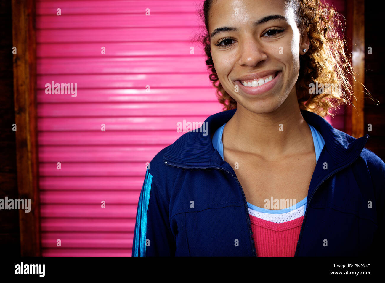 Young female runner wearing a pony tail stands in front of a pink door ...