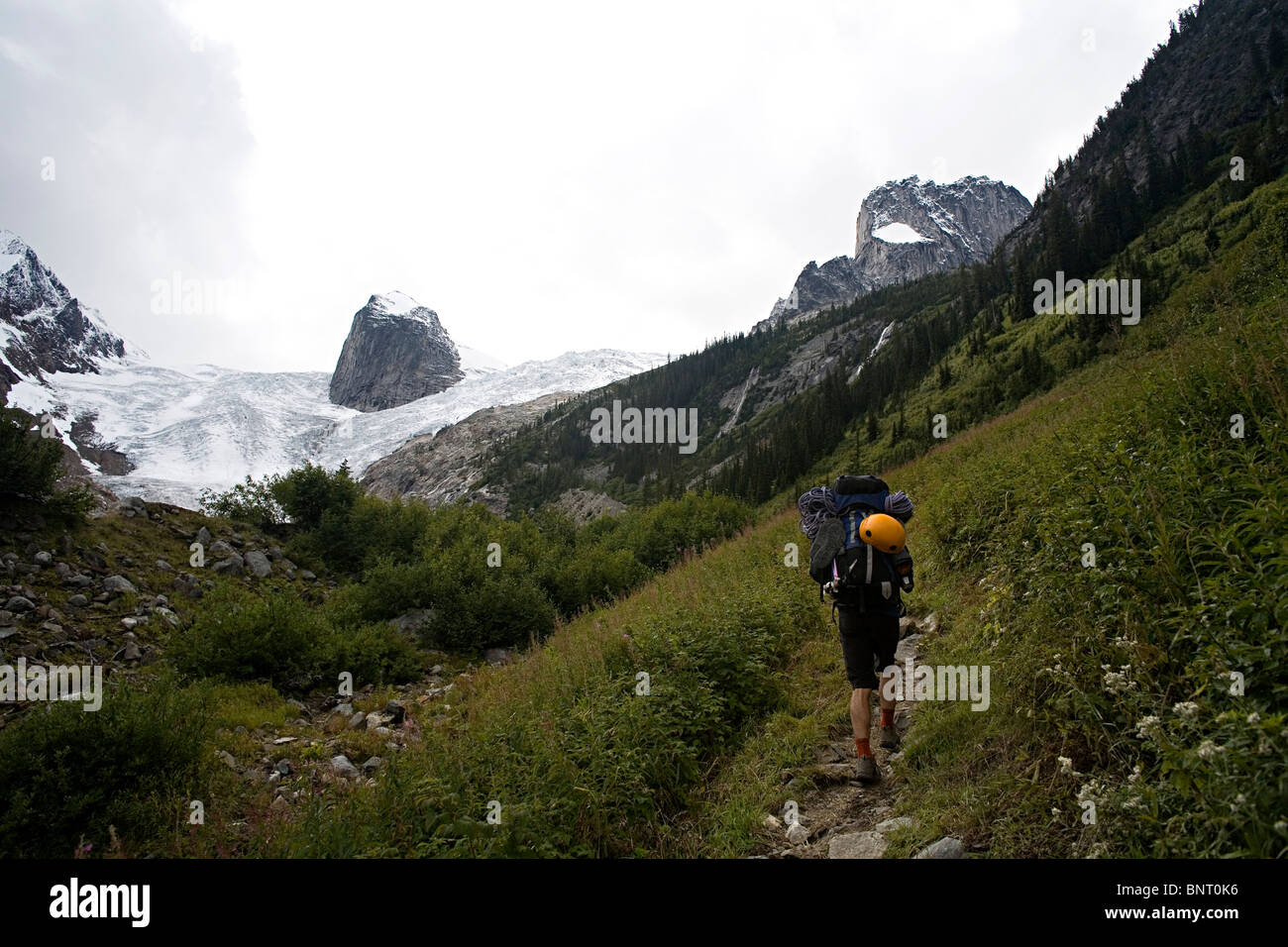 Man carrying a large backpack with a yellow climbing helmet attached to ...