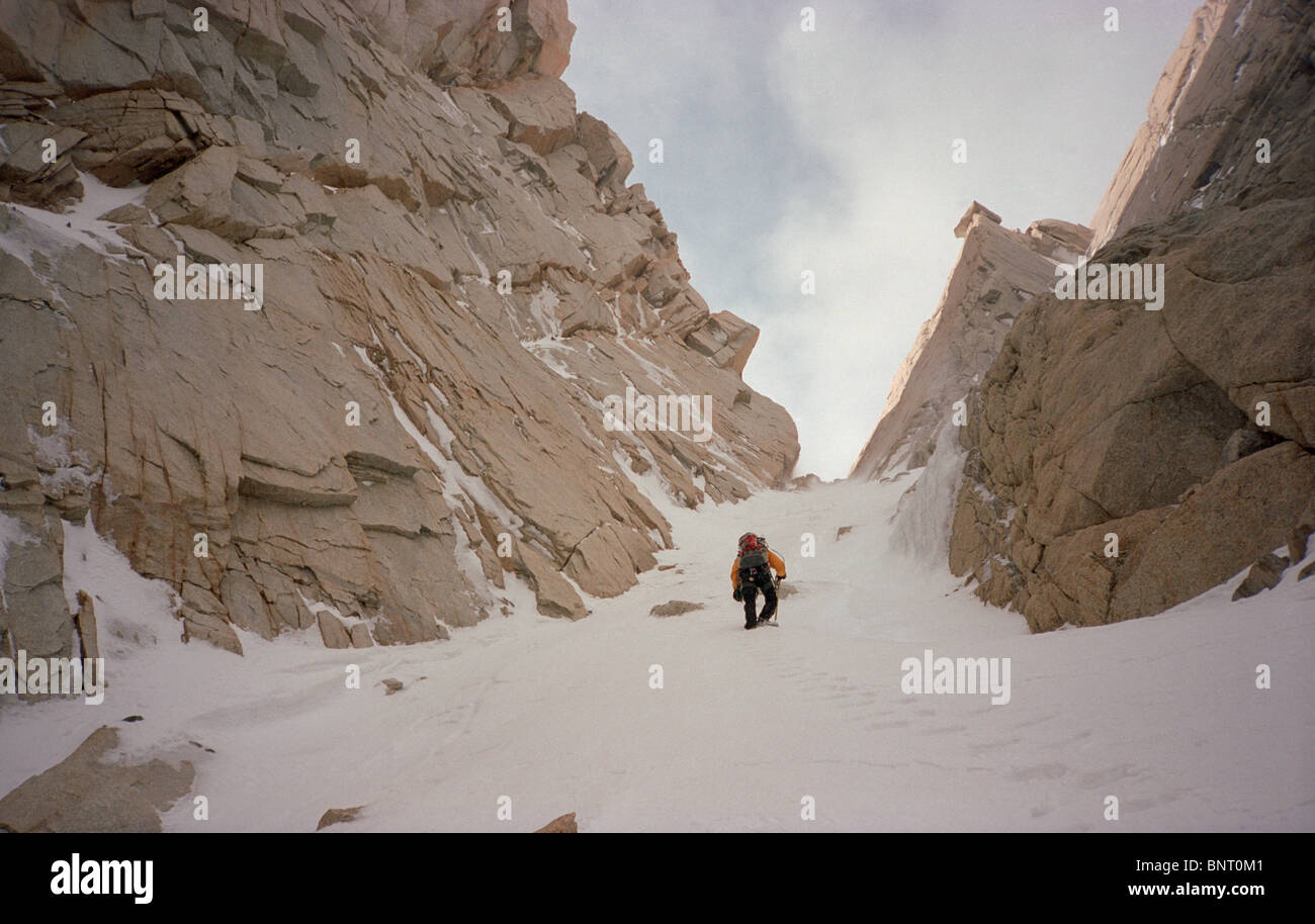 Mountain climber in yellow jacket ascends steep snow gully Stock Photo ...