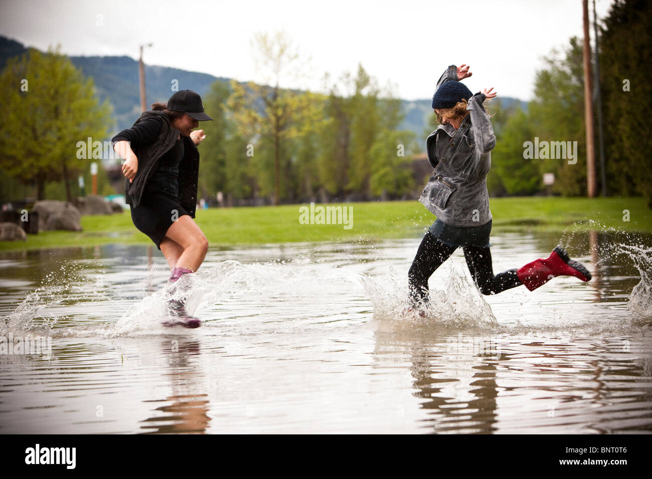 Two young women splash each other in a large puddle Stock Photo - Alamy