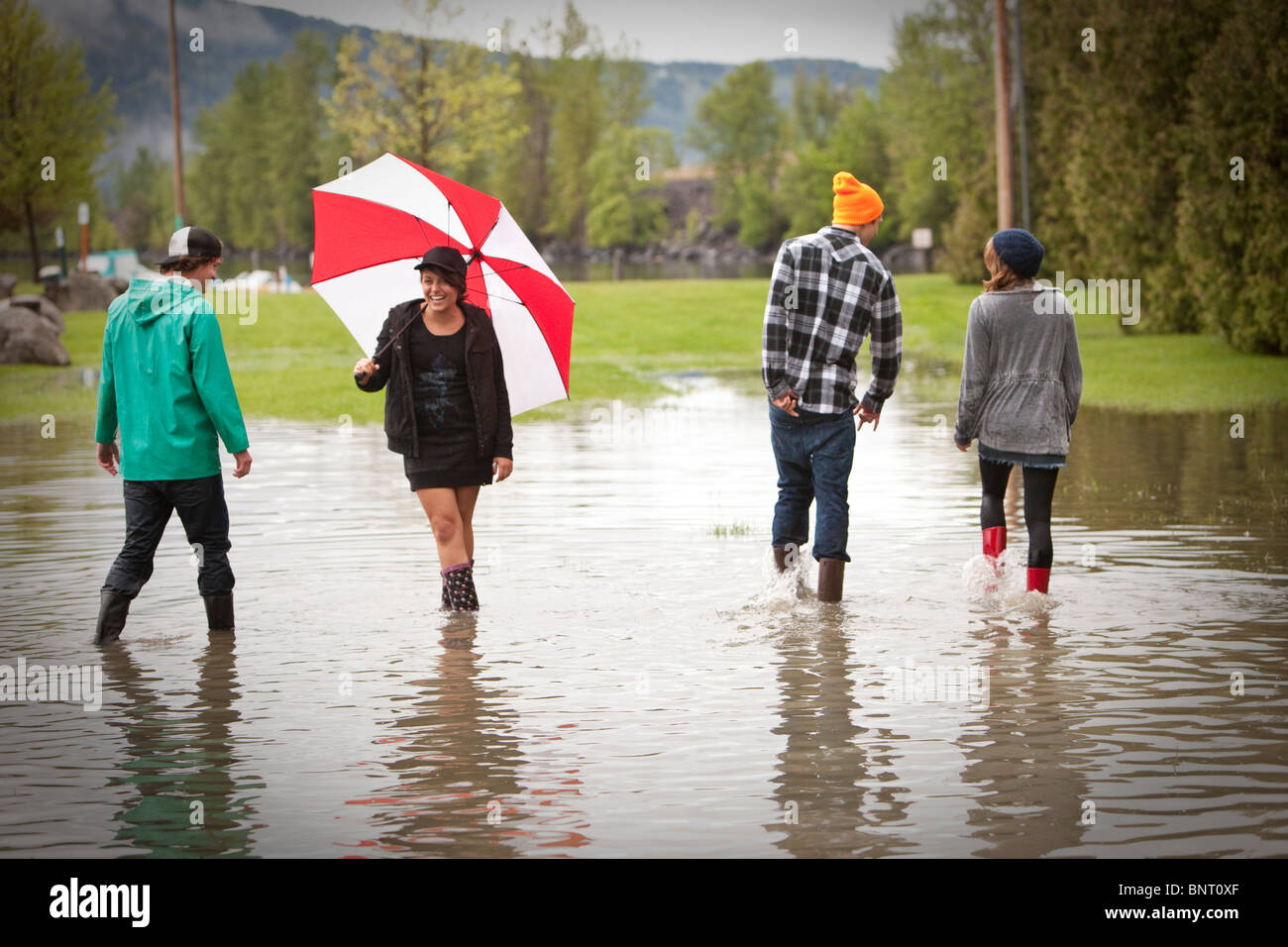 Two young adult couples smile while walking through a large puddle ...