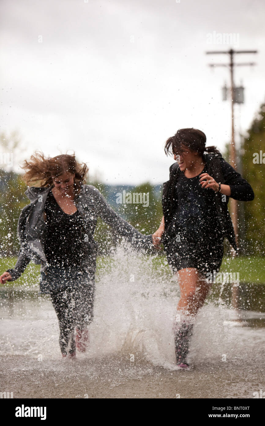 Two young women smile while running through a large puddle Stock Photo ...