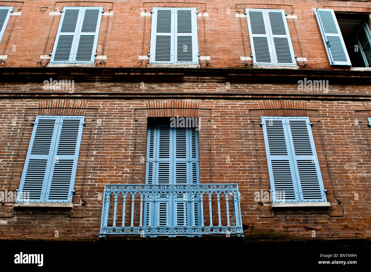 Red brick house with blue balcony and closed shutters, Toulouse, France ...