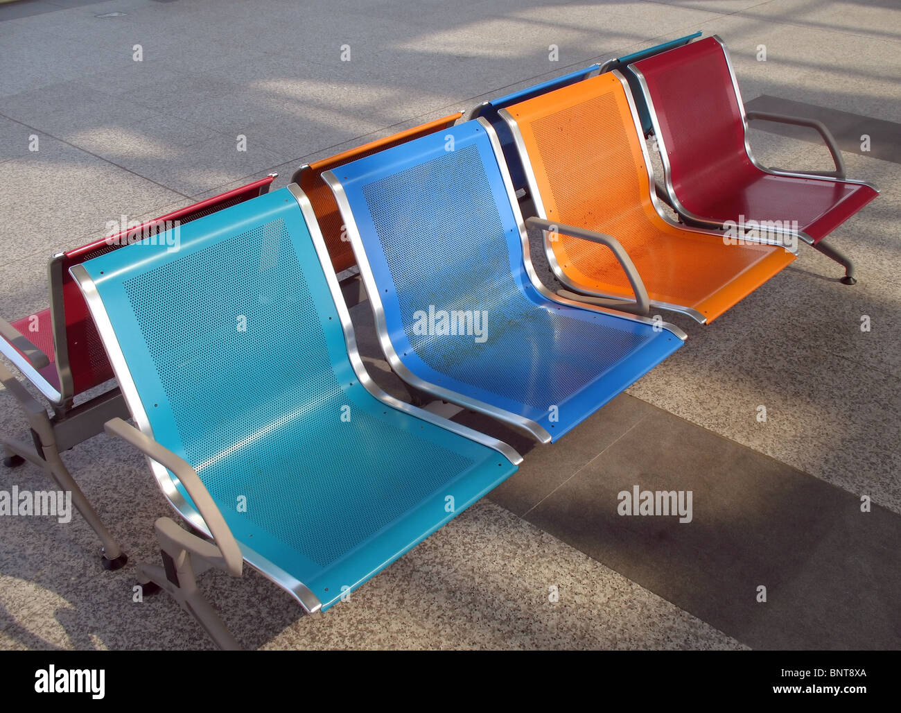 A modern bench made fro multi-colored steel, on the platform of a train ...