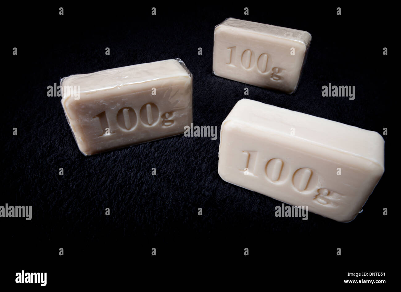 Three bars of plain soap stamped with 100g on a black towel Stock Photo ...