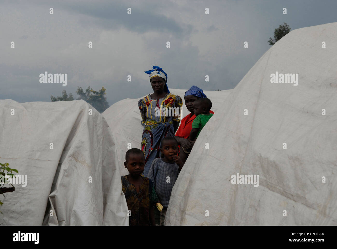 Displaced Congolese women stand with their children amid straw huts ...