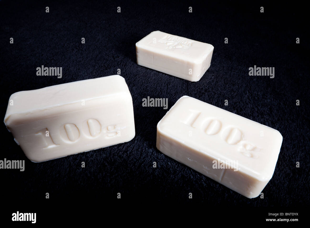 Three bars of plain soap stamped with 100g on a black towel Stock Photo ...