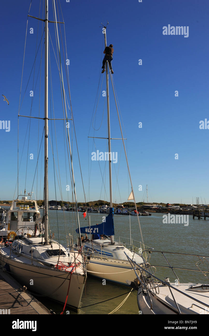 man working up a mast on board a yacht moored in Littlehampton harbour ...