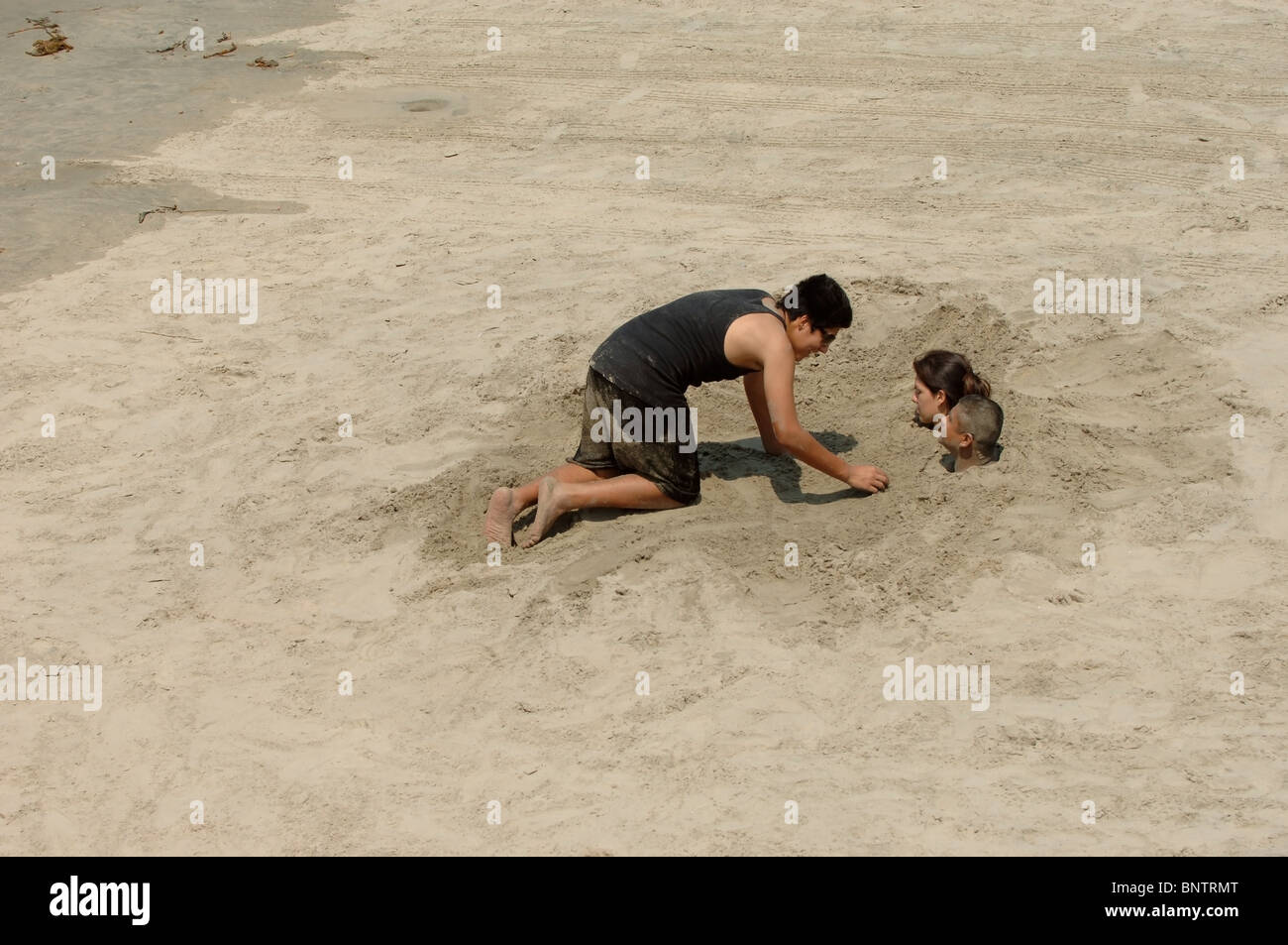 Young couple buried in the sand up to their necks by another friend ...