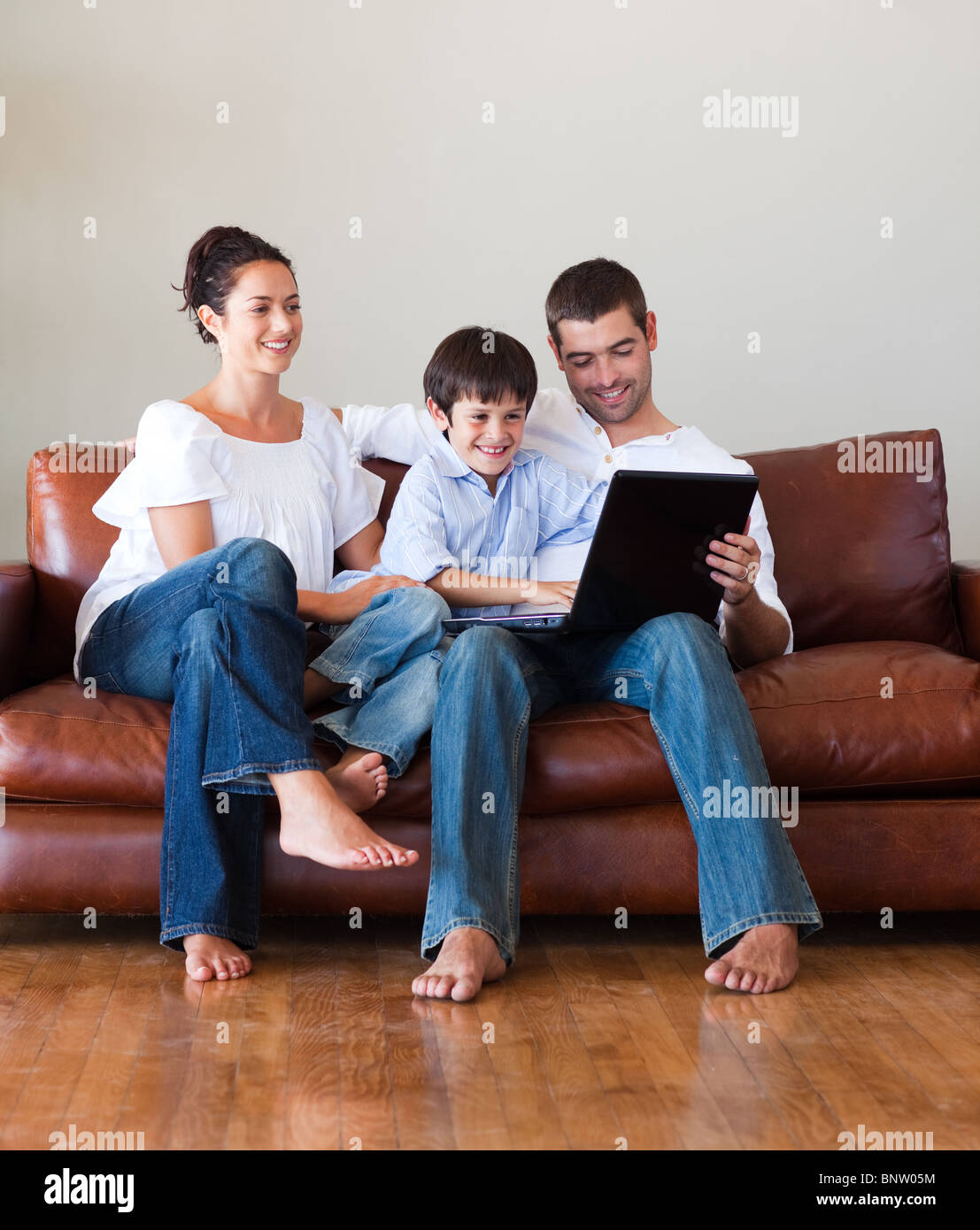 Parents and kid playing with a laptop on a couch Stock Photo - Alamy