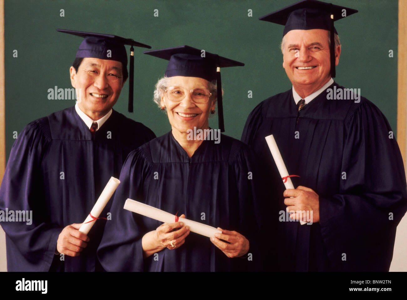 Three adult students wearing graduation gowns Stock Photo - Alamy