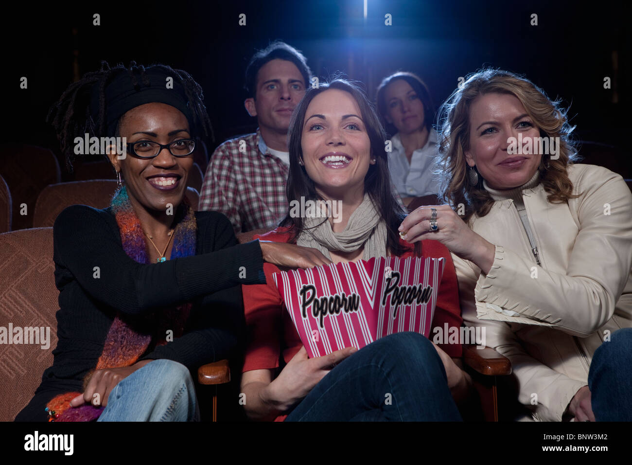 Three woman sharing popcorn in movie theatre Stock Photo - Alamy