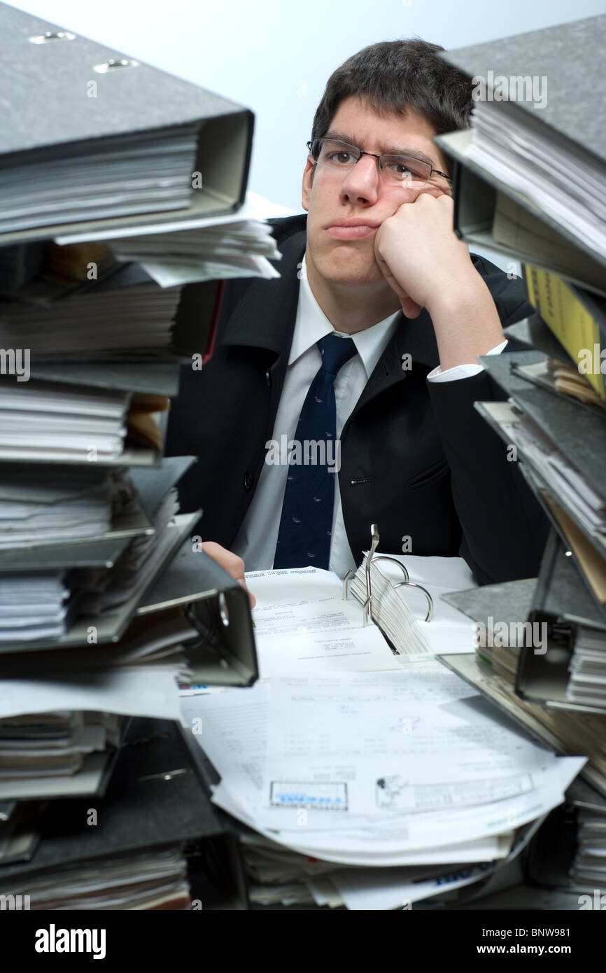 A confused man sitting amidst piles of binders Stock Photo - Alamy