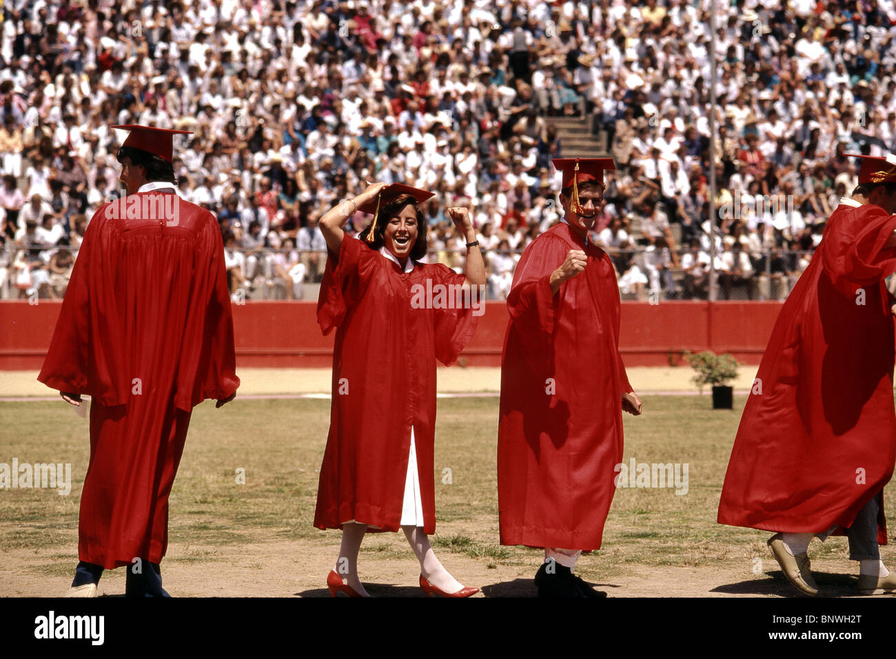 Triumphant high school seniors in red caps and gowns march at their ...